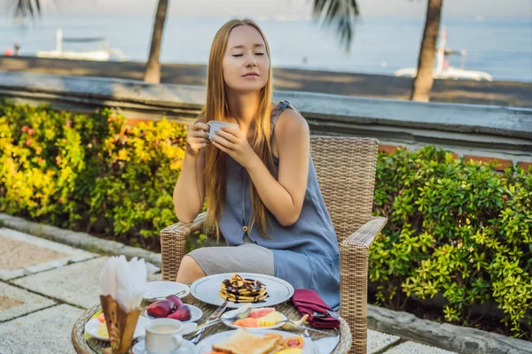 Young woman having romantic breakfast in sunrise at resort restaurant ...