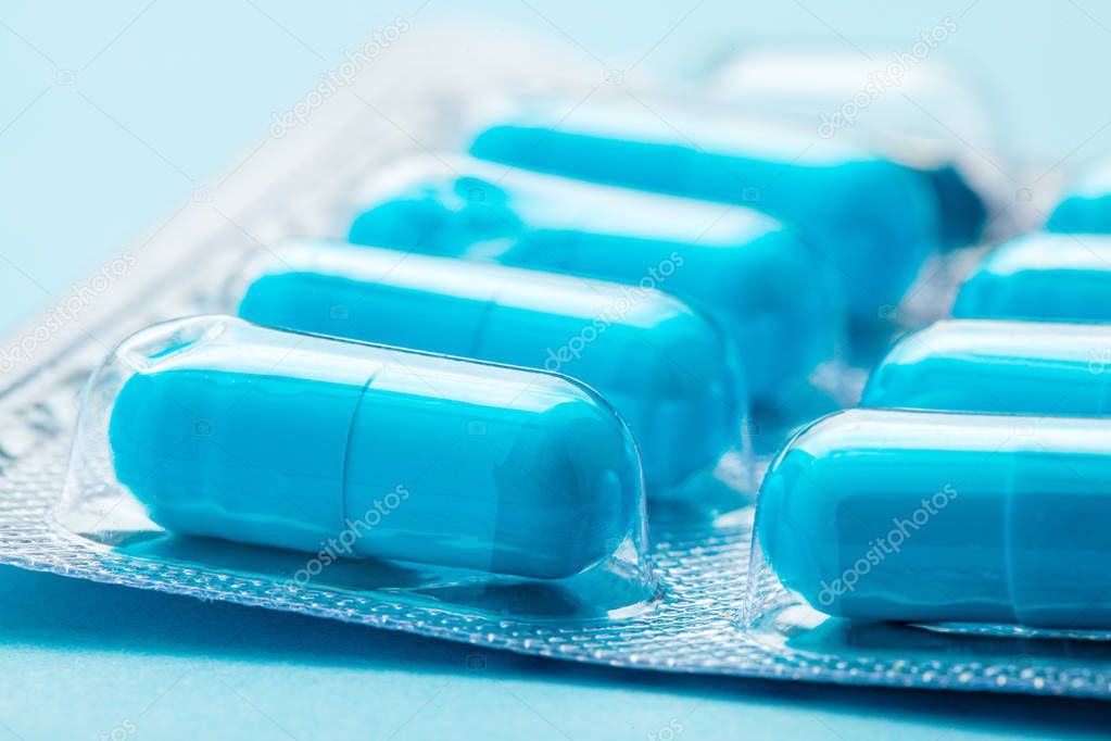 Comprimidos azules en cápsulas. Una cápsula está abierta. Fondo azul 2024