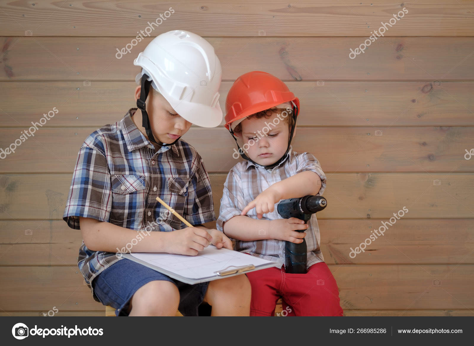 Two cute boys in construction helmets are discussing a plan for the ...