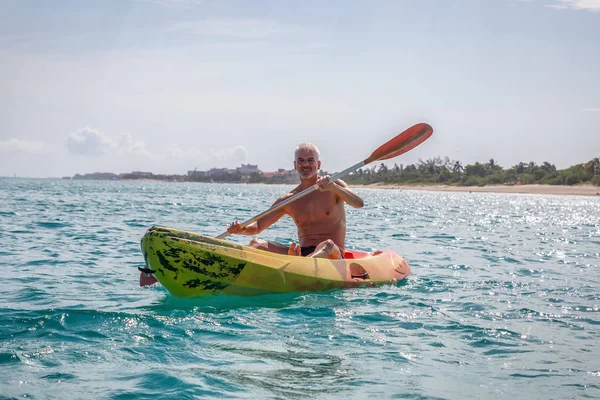 Elder fit man is kayaking on a bright yellow kayak in Caribbean Sea ...