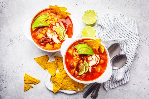 Mexican soup with beans, chicken, corn and nachos in white bowls, top ...