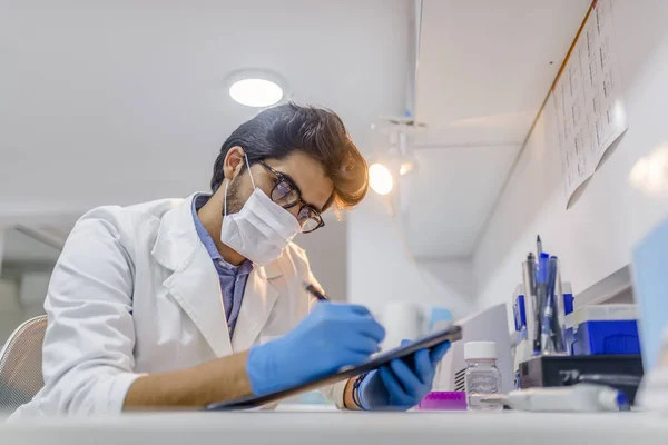 Young male lab technician works on some samples and make notes on ...