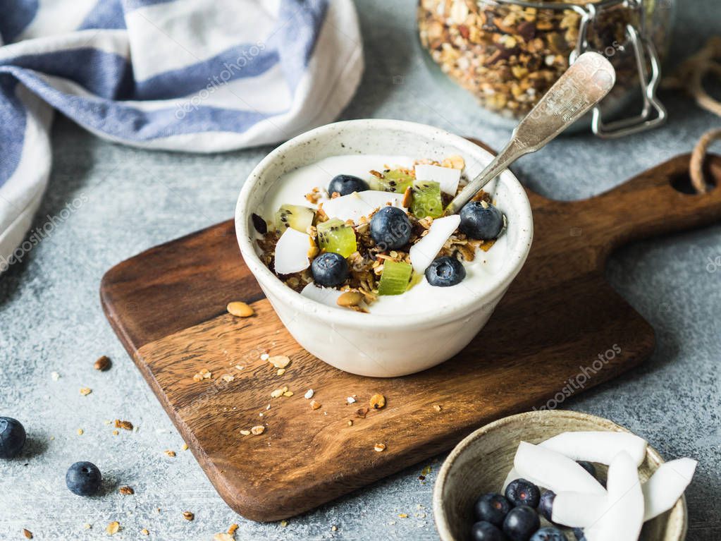 Granola casera con yogur, arándanos, kiwi, coco en un tazón blanco ...