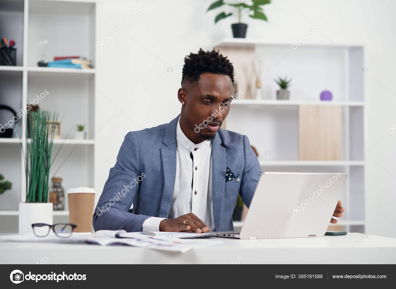 Serious dark-skinned young office manager works with different reports ...