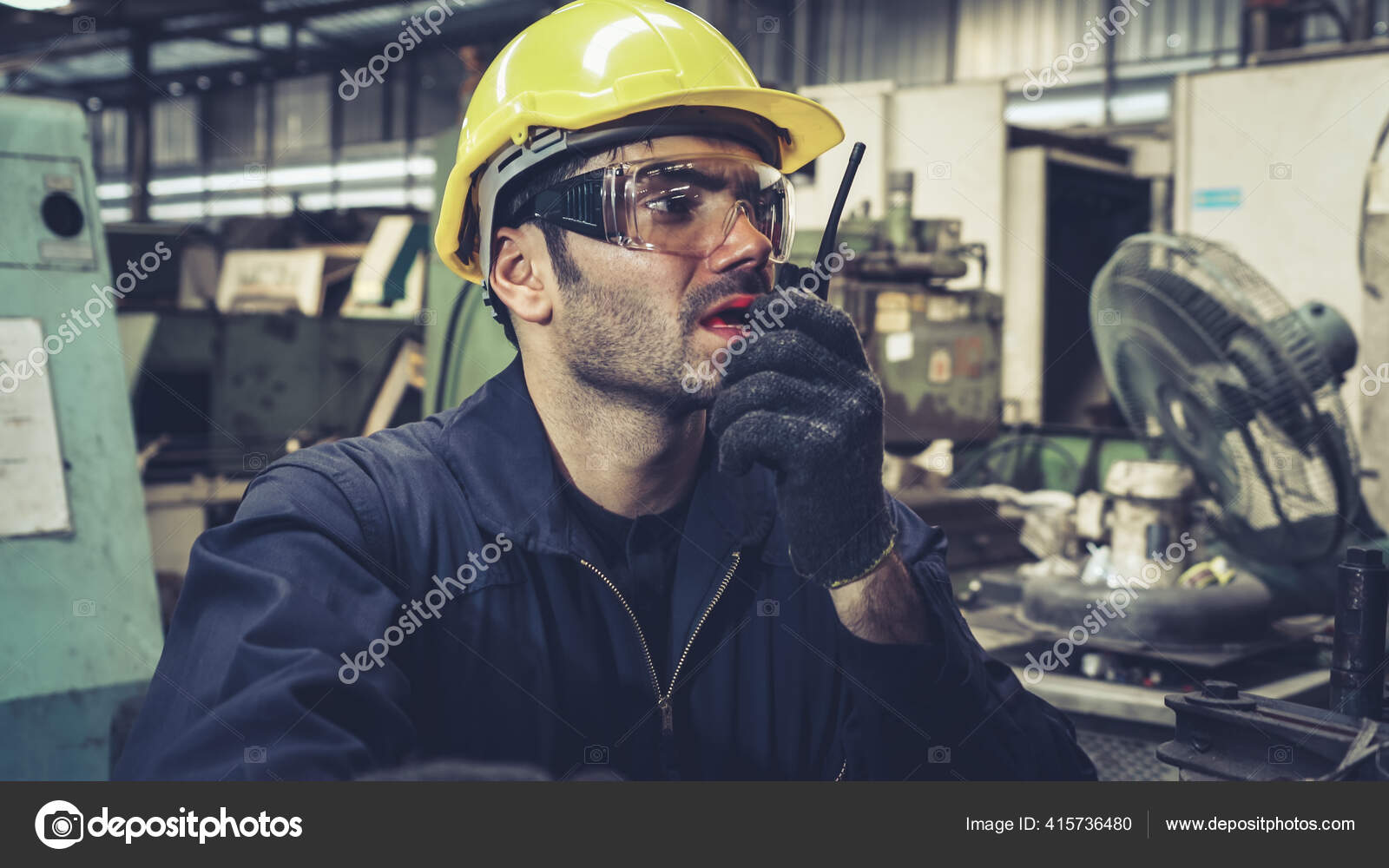 Factory worker talking on portable radio while inspecting machinery ...